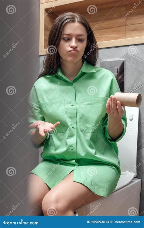 Young Woman Sitting On The Toilet Has Run Out Of Toilet Paper Stock