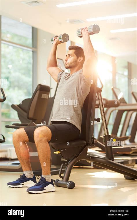 Full Length Portrait Of Handsome Muscular Man Working Out In Gym Using
