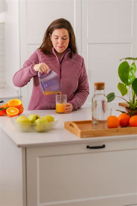Attractive Young Brunette Girl Pouring Freshly Squeezed Orange Juice Into A Drinking Glass Stock