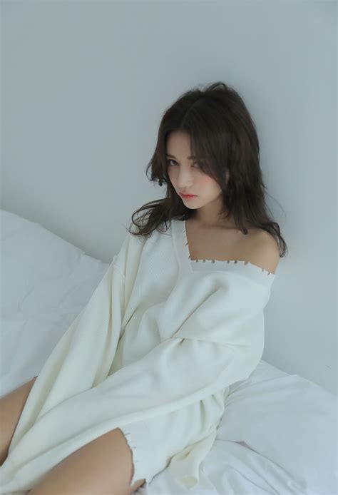 A Woman Sitting On Top Of A Bed Wearing White Clothing And Posing For