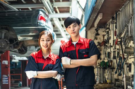 아시아 자동차 엔지니어 사람들은 정비사 차고에서 헬멧 작업을 착용합니다제복을 입은 젊은 자동차 정비사는 카메라를 보고 웃으며