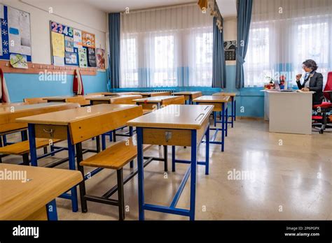 Empty Class Room With Wood Tables And Female Teacher Sitting At Her