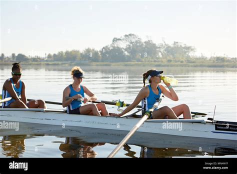 Female Rowing Team Resting Drinking Water In Scull On Sunny Lake Stock