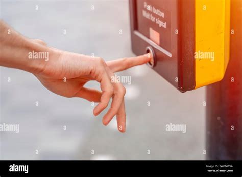 Hand Of Pedestrian Pressing The Traffic Light Control Button To Safely Cross The Street