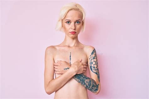 Young Blonde Woman With Tattoo Standing Shirtless Relaxed With Serious