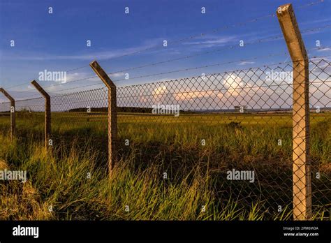Wire Mesh Fence And Barbed Wire With Grass Field And Blue Sky Clouds