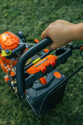 오렌지색 잔디 깎는 기계의 손잡이를 잡고 있는 손의 클로즈업 위에서 본 모습 잔디 깎는 기계는 잔디밭에서 작동하여 장비의 세부 사항과 잔디 깎기 동작을 강조합니다 광고에