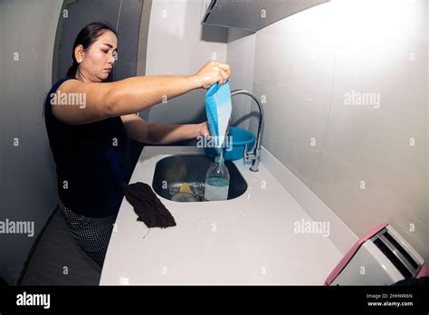 An Asian female maid is pouring detergent in the kitchen sink on ...