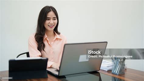 한 젊은 여성이 사무실 책상에 앉아 노트북으로 작업하고 있습니다 그녀는 밝고 현대적인 작업 공간에서 사무실 문서와 커피 머그잔을 옆에 두고 집중하고 참여하고 있는 것처럼