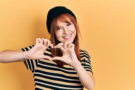 Redhead Young Woman Wearing Wool Cap Smiling In Love Showing Heart Symbol And Shape With Hands