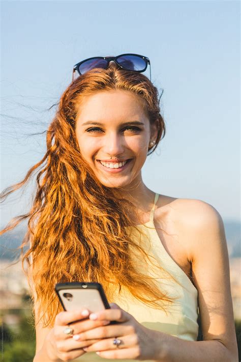 Young Redhead With Long Hair Using Mobile Phone Outdoors By Stocksy Contributor Giorgio