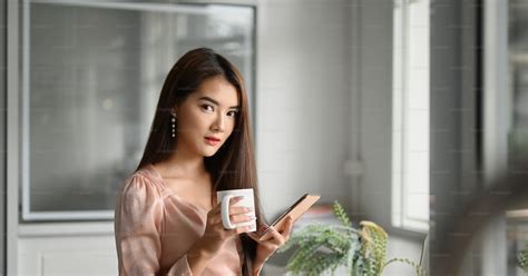 커피 컵과 스마트폰을 들고 카메라를 바라보는 아시아 여성의 초상화 사진 Unsplash의 초상 이미지