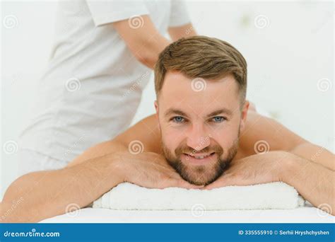 Female Masseur With Long Hair In White Uniform Doing Back Massage To Man Lying On Couch In