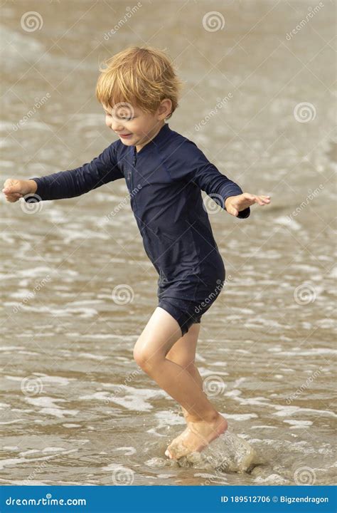 Young Boy With Blonde Hair And Navy Swimsuit Having Fun Splashing At