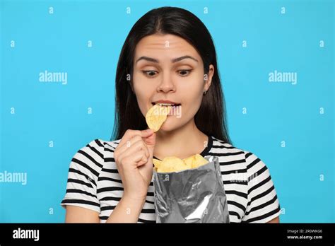Beautiful Woman Eating Potato Chips On Light Blue Background Stock