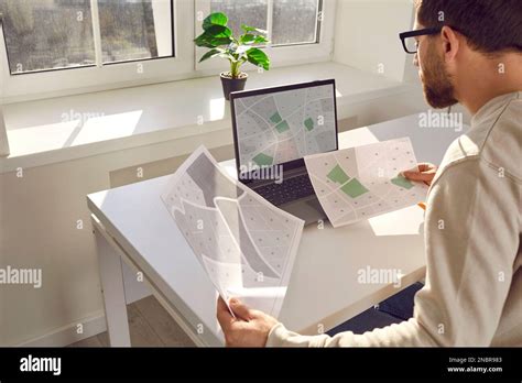 Serious Engineer With Cadastral Maps And Projects Is Sitting At Desk