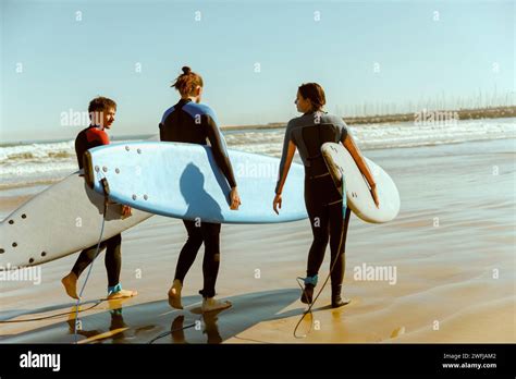 Back View Of Surfers With Surfboards In Wetsuit Are Walking On The