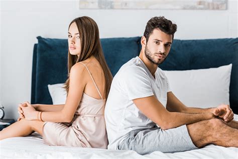 Young Frustrated Couple In Pajamas Sitting On Bed Back To Back And